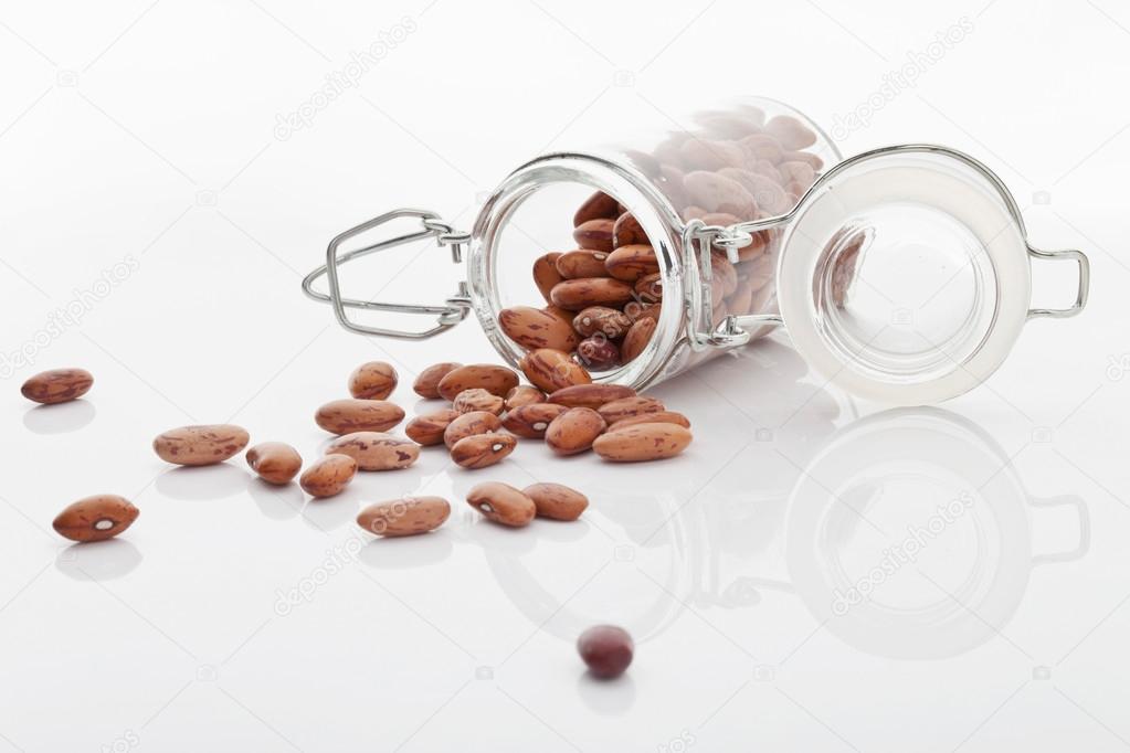 Frijoles secos en frasco de vidrio derramándose sobre fondo blanco 2024