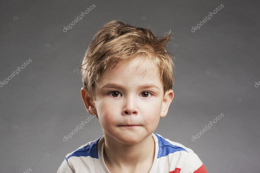 Attentive young boy looking at camera against gray background, portrait ...