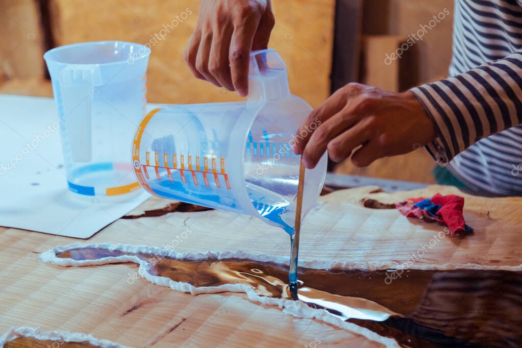 Primer plano del carpintero vertiendo l quido epoxi en una mesa de madera. Proceso de fabricaci ...
