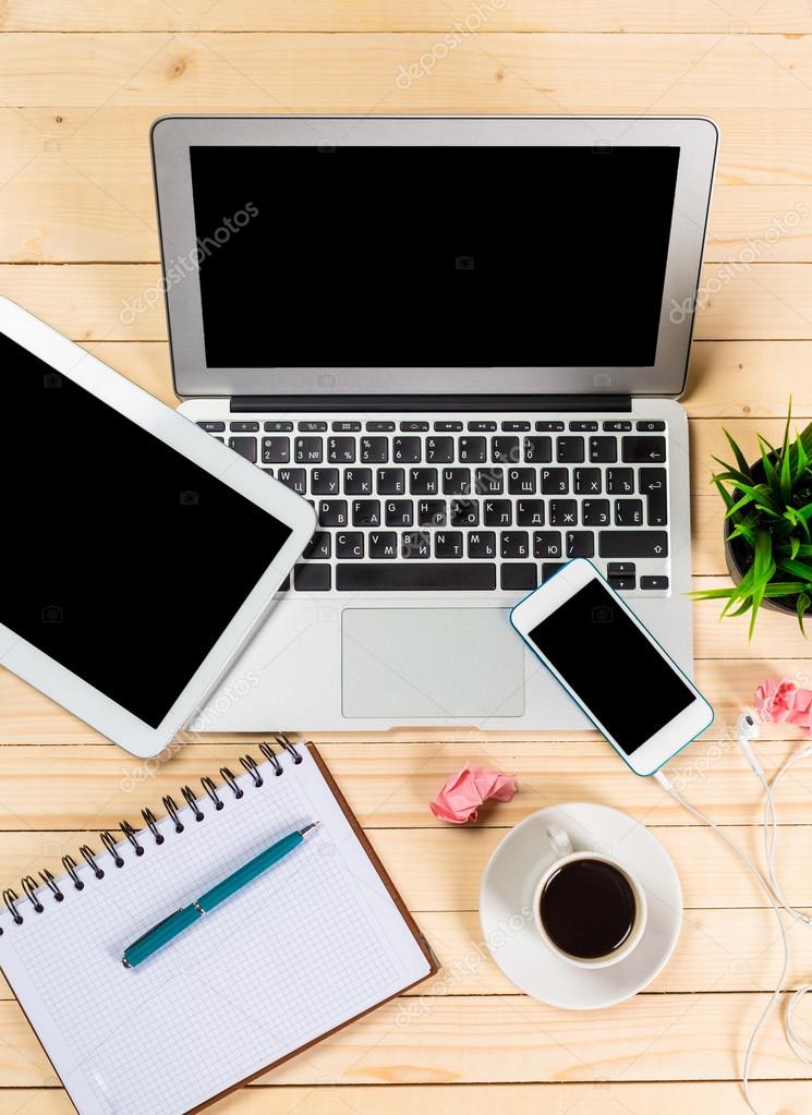 Tableta, bloc de notas, computadora y taza de café en la mesa de madera ...