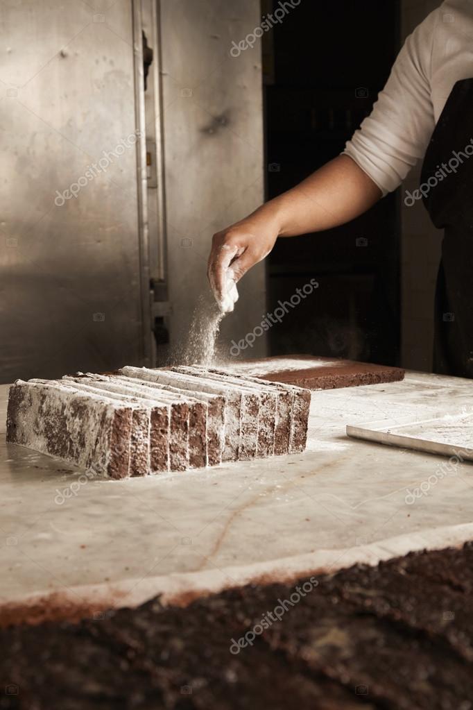 Black man chief pours sugar powder on chocolate cakes before packaging ...