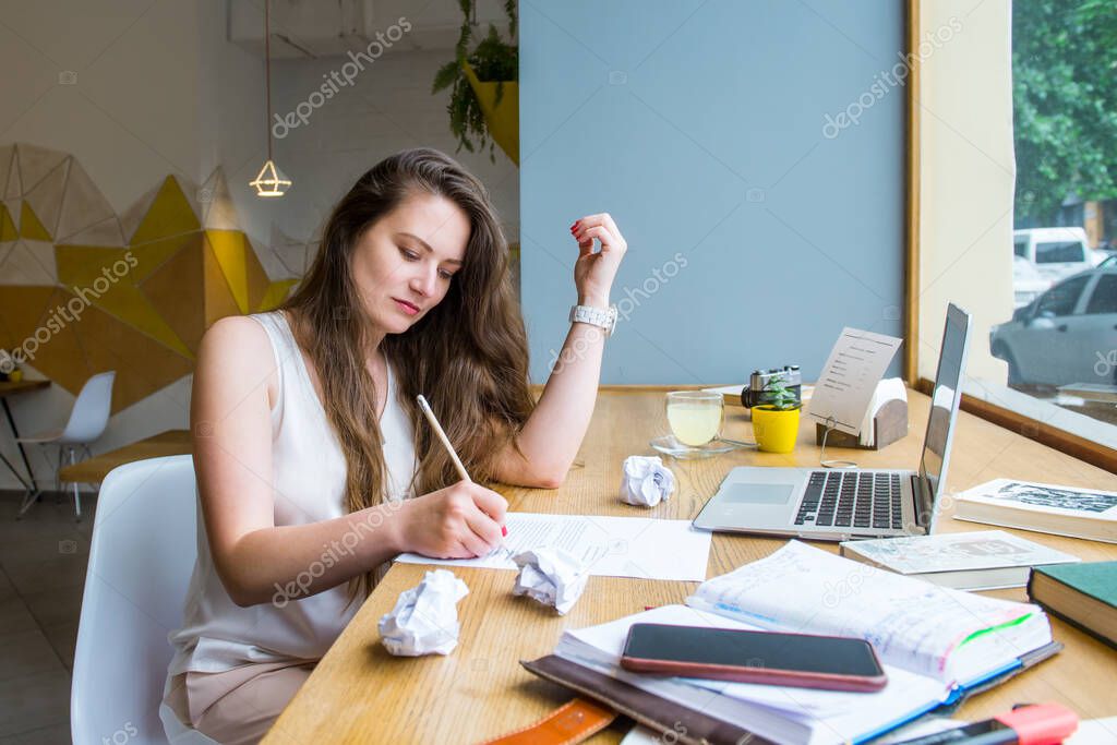 Mujer joven concentrada haciendo notas en papel mientras trabajaba en su computadora portátil en ...