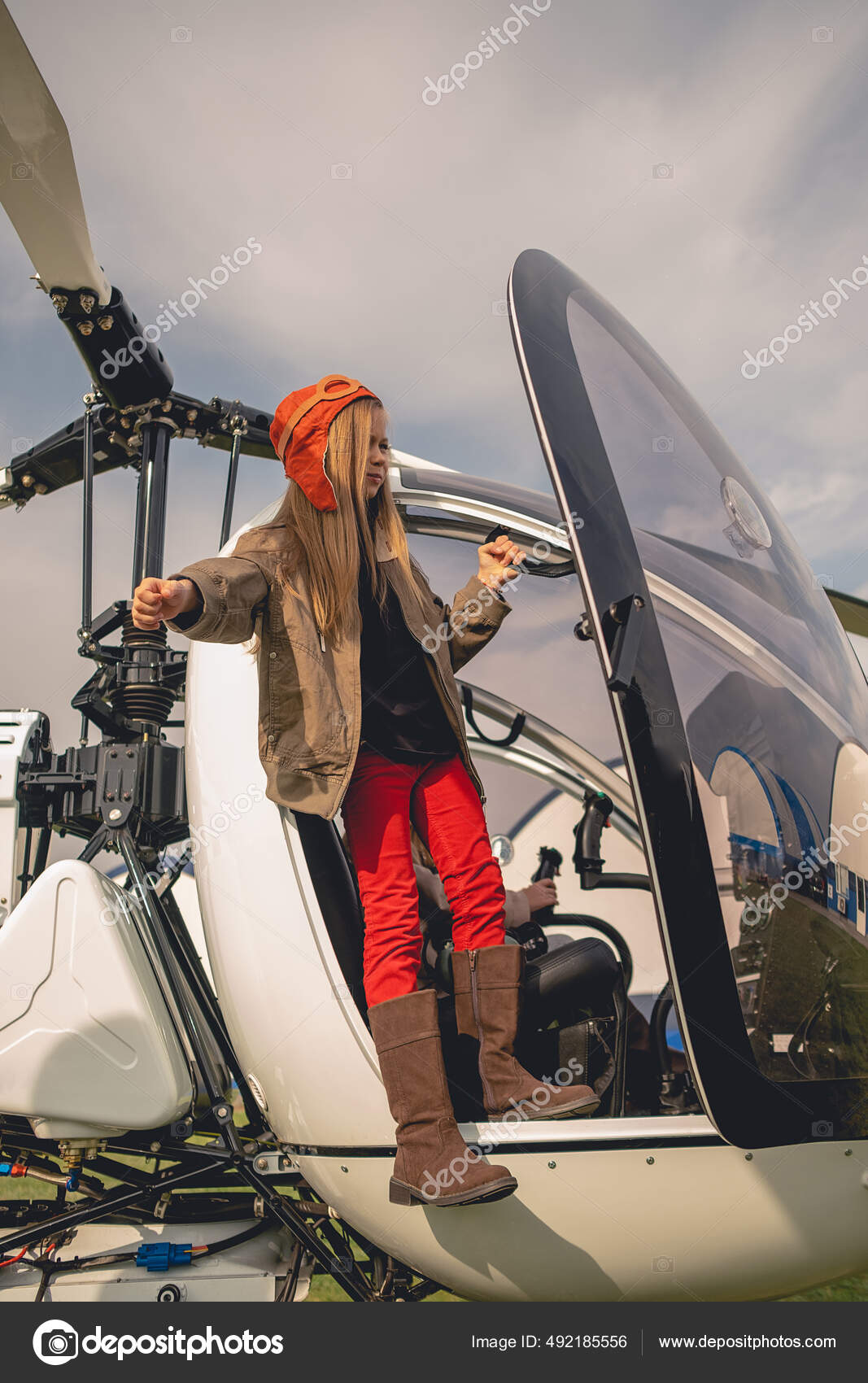 Tween girl in pilot hat looking into distance from helicopter cockpit ...