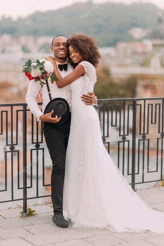 Happy black bride and groom softly hugging on the terrace with ...