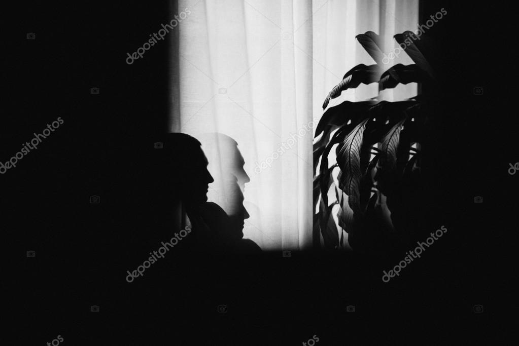 Mysterious man sitting with shadows by the window. Dark background ...