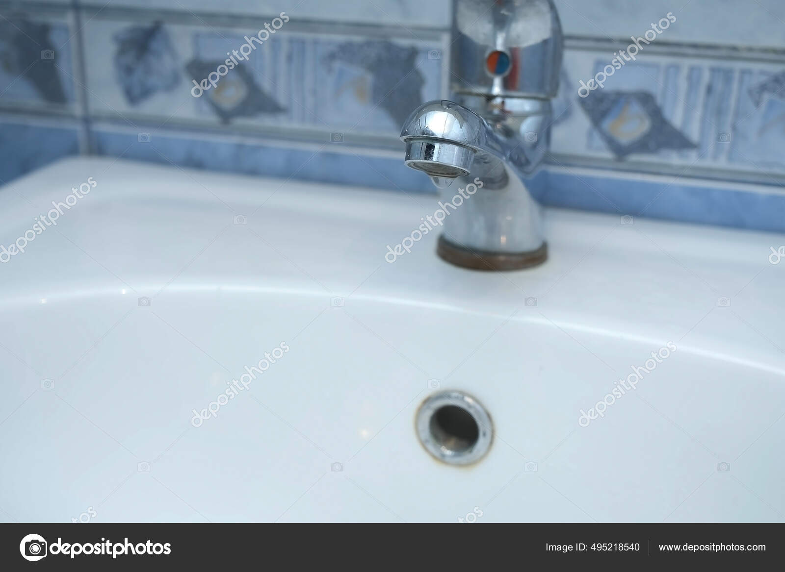 Water dripping from a faucet into white sink in bathroom, close-up view ...