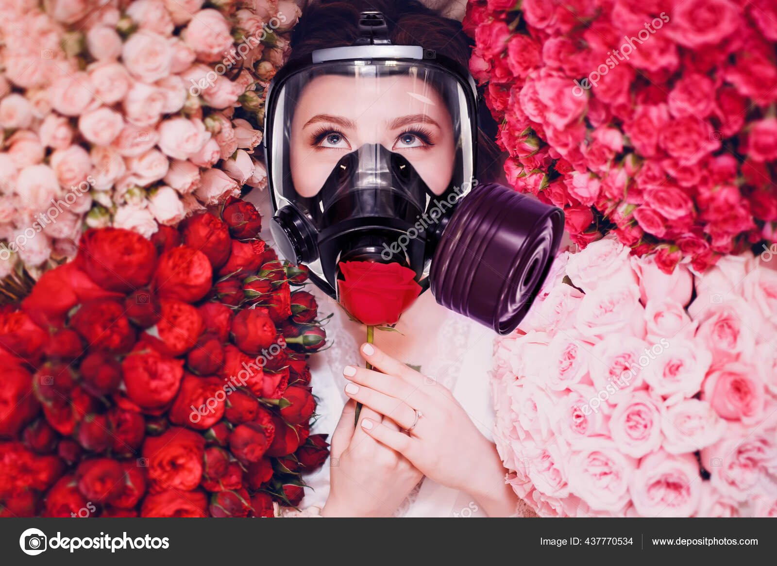 Woman with unrecognizable face sniffing flower in a gas mask ...