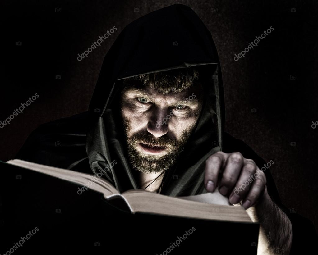 Necromancer casts spells from thick ancient book by candlelight on a ...