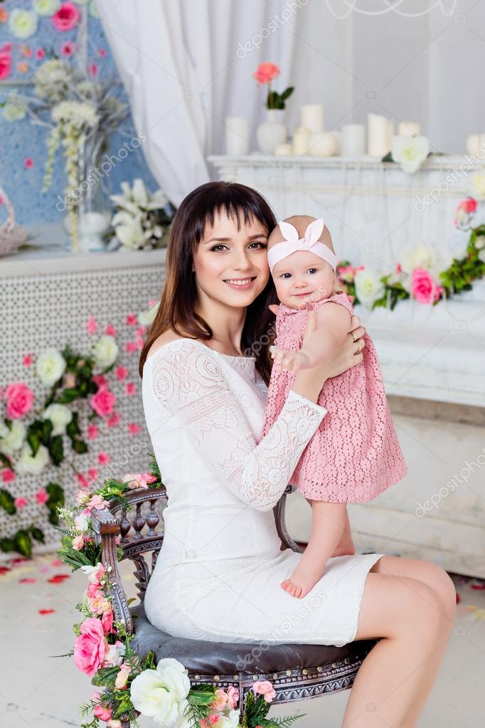 Beautiful and happy mom brunette in a white dress holding on the ...