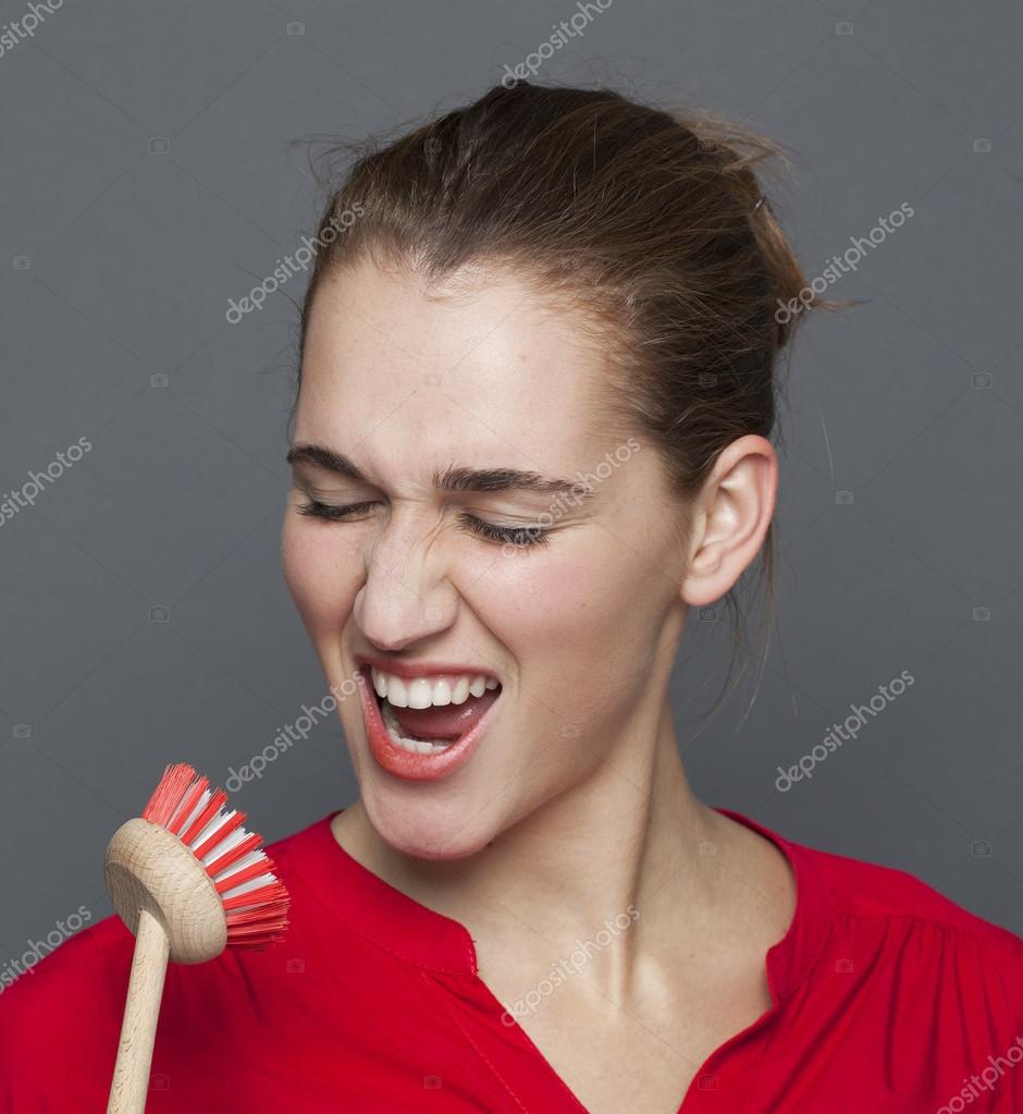 Excited young cleaning lady singing on a dish brush microphone Stock ...