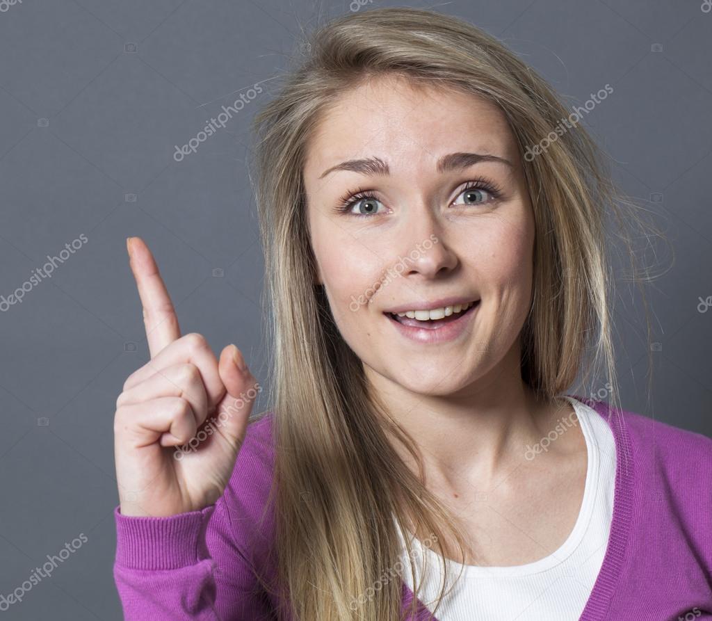 Ecstatic young woman raising her finger for speaking up with bright ...