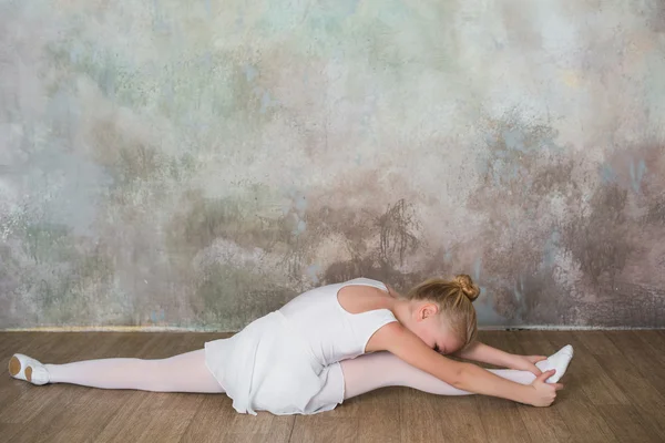 Little ballet dancer doing stretching before class in a white bathing ...