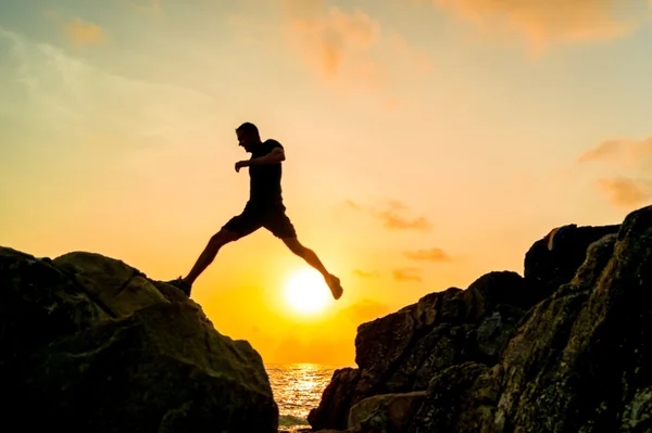 Silhouette of a man standing on a rock on the sunset and sea background ...