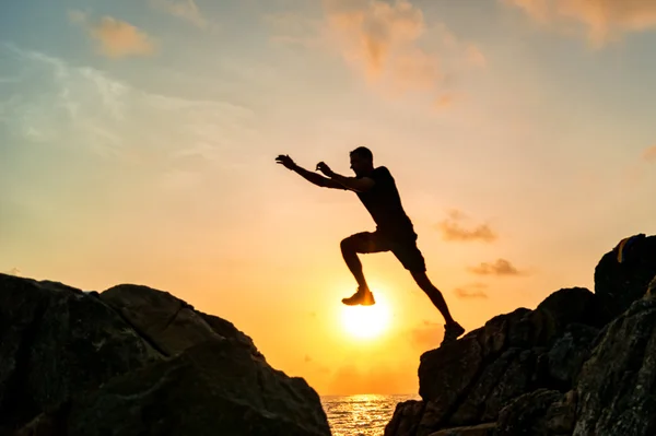 Silhouette of a man standing on a rock on the sunset and sea background ...