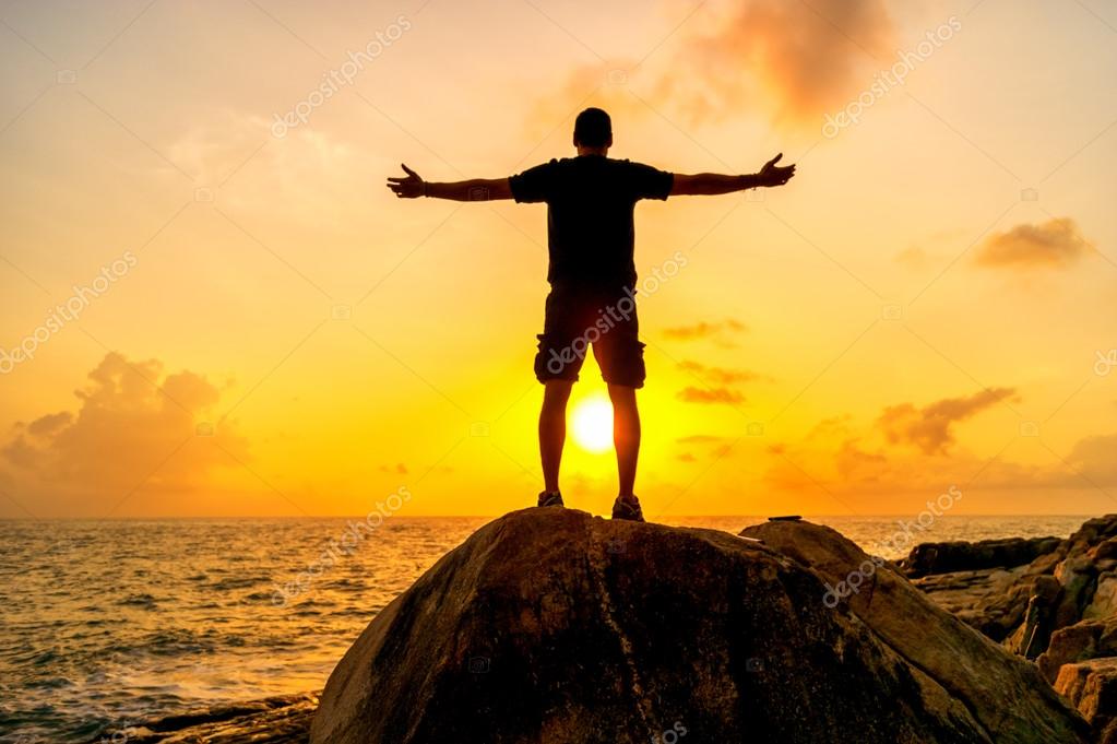 Silhouette of a man standing on a rock on the sunset and sea background ...