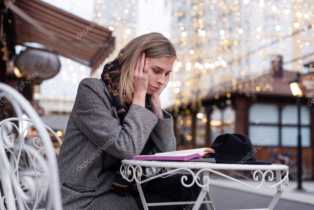 Una joven hermosa se sienta en una mesa en un café de la calle y se ...