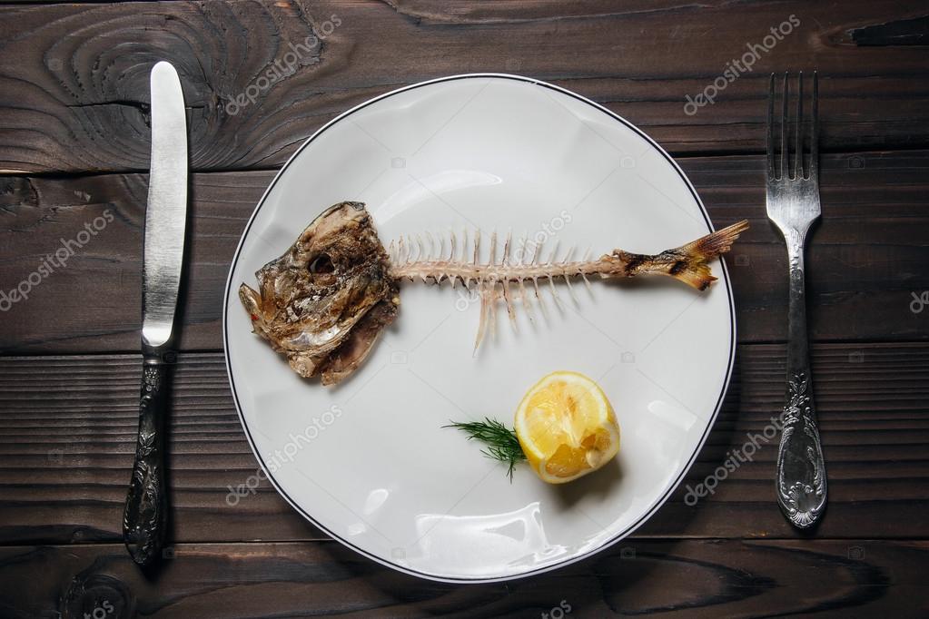 Fishbone on plate and squeezed lemon, knife and fork Stock Photo by ...
