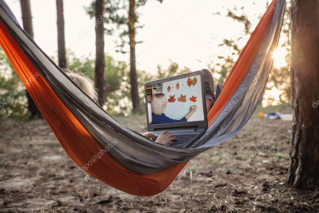 Lindo niño usando gadget digital para leer y aprender en la hamaca en el bosque salvaje ...