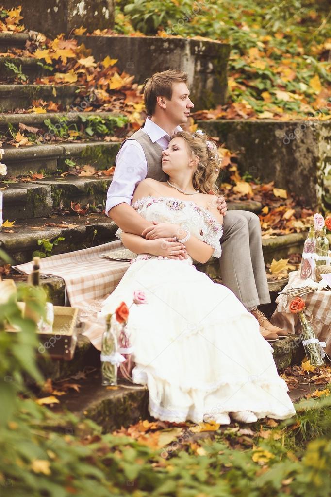 The bride and groom in a rustic style sitting on stone steps at sunny ...