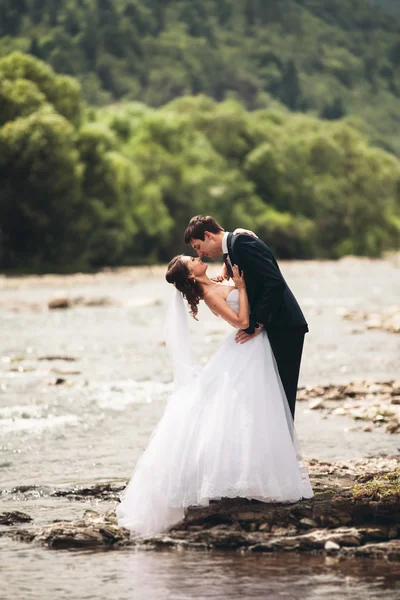 Elegant gentle stylish groom and bride near river with stones. Wedding ...