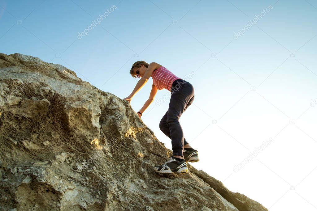 Mujer excursionista escalando empinada roca grande en un día soleado ...
