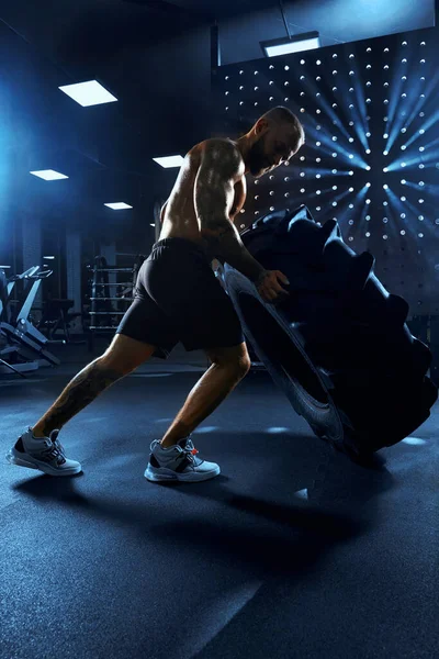 Man moving giant tire wheel in gym. - Stock Image - Everypixel