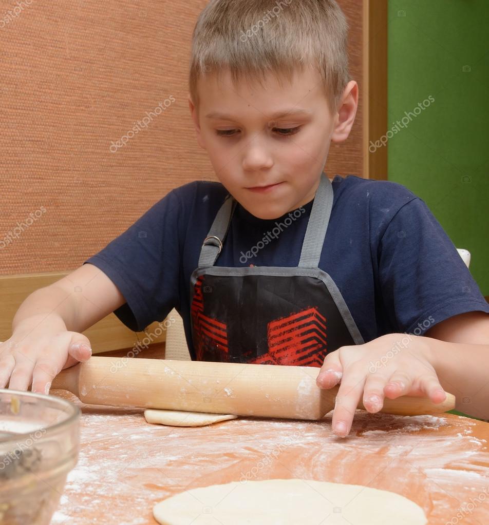 Young boy rolling dough with a large wooden rolling pin as he prepares ... Young boy rolling dough with a large wooden rolling pin as he prepares ...
