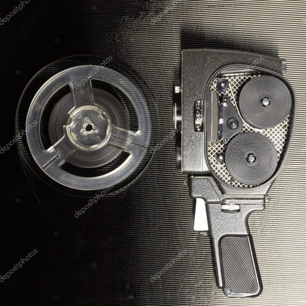 Старая любительская кинокамера и катушка пленки на черном фоне ...