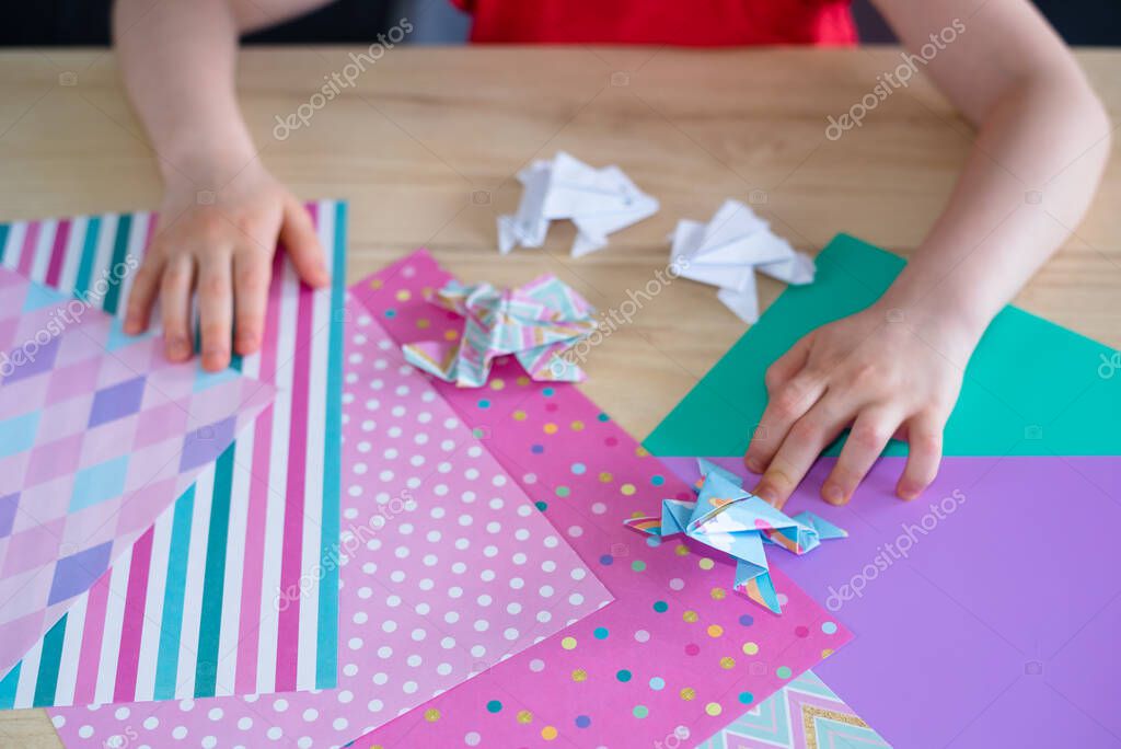 Una niña en edad preescolar hace una rana de origami con papel ...