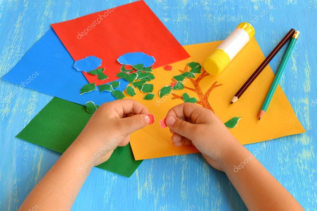 Child tears a red paper into small pieces. Child holds colored paper in ...