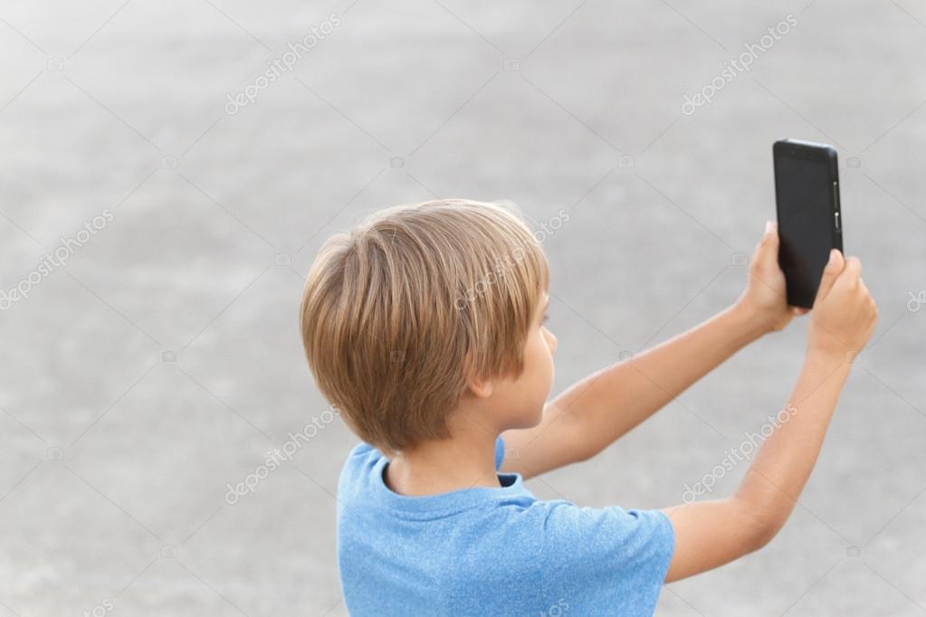 Boy using mobile phone. Child taking photo with his smartphone. Gray ...