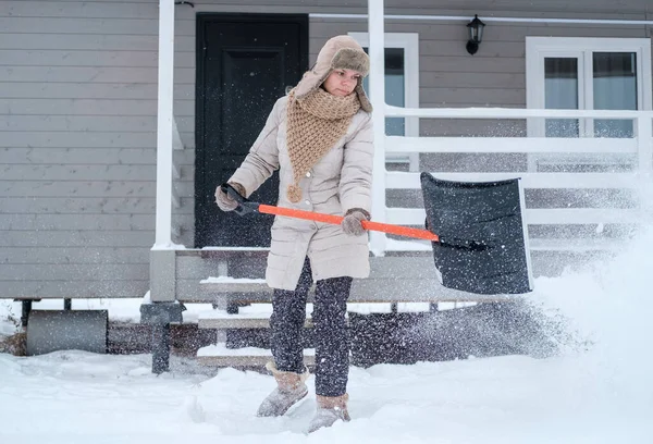 clearing snow near the house after a heavy snowfall. a young woman ...